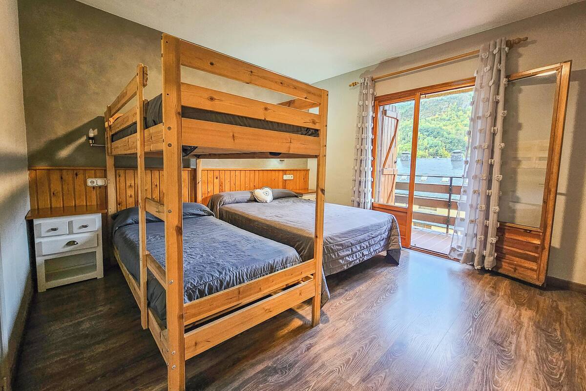 Quarto com beliche, uma pequena mesa de cabeceira e janela com cortinas.