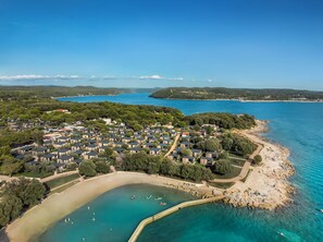 Vista aérea de uma área residencial costeira, com casas, uma praia e águas azul-claras.