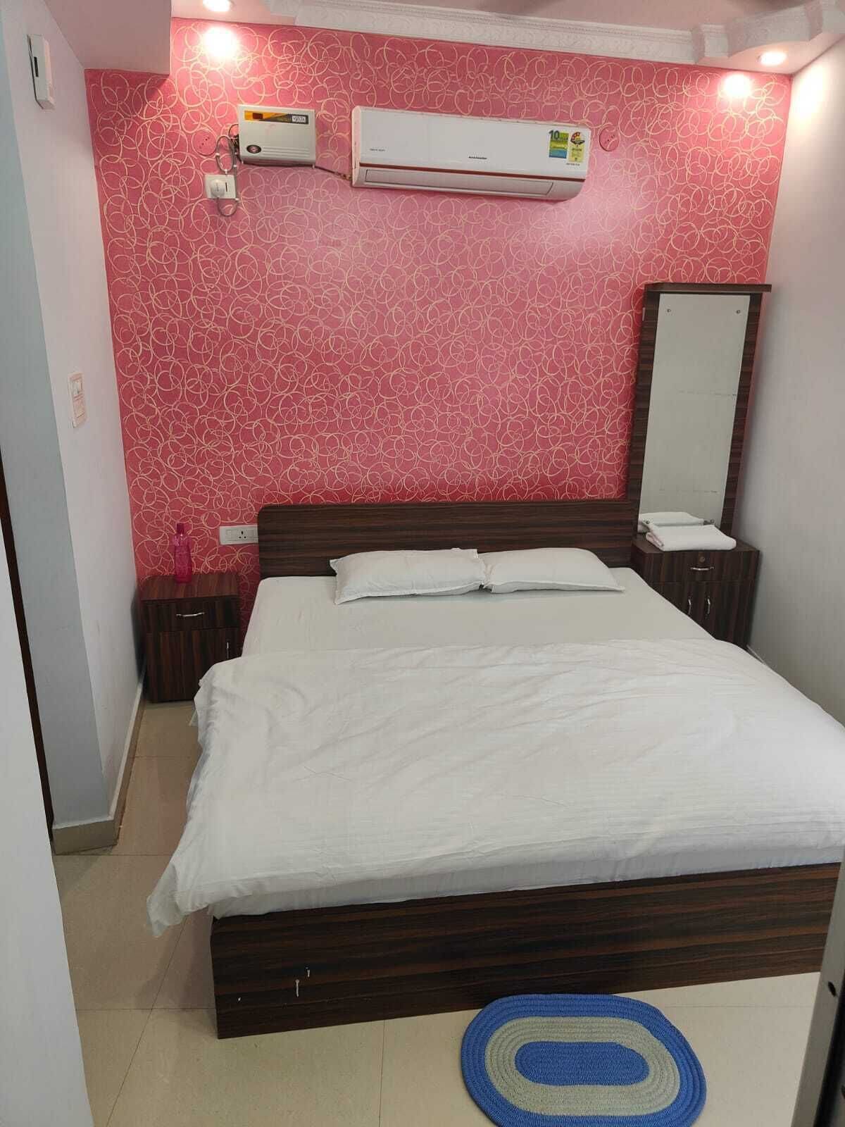 Quarto com cama, mesa de cabeceira, cômoda, espelho e ar condicionado na parede.