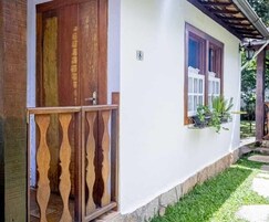 Uma casa com fachada branca, porta de madeira e janela com planta do lado de fora.