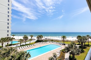 Um hotel com piscina, vista para a praia e palmeiras.