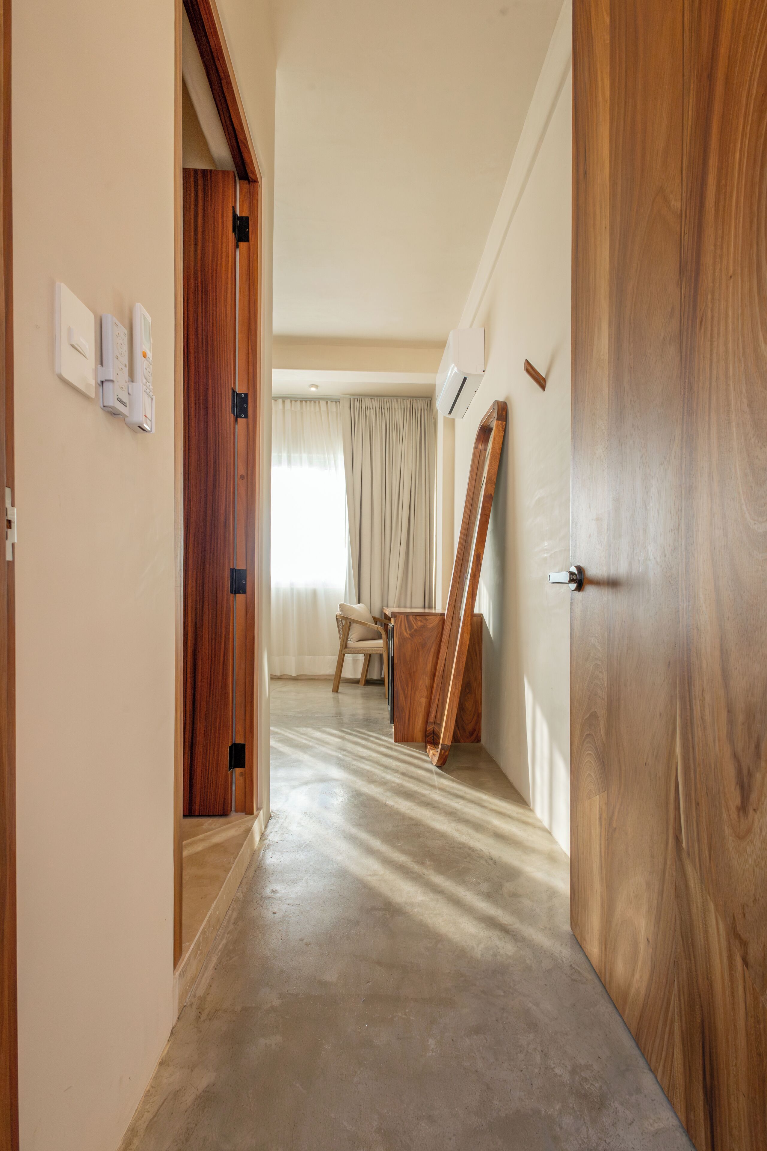 Um corredor com uma porta de madeira, uma cadeira e um espelho grande encostado na parede.