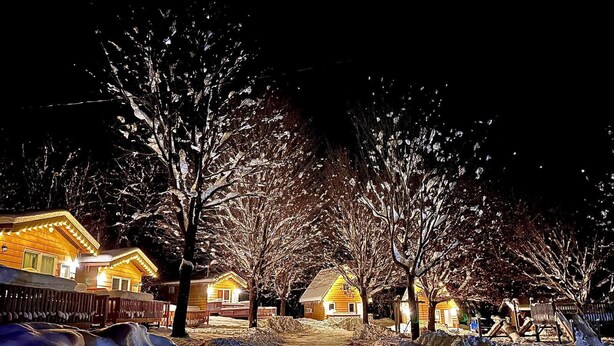 Uma passagem coberta de neve que leva a uma fileira de casas de madeira com iluminação acolhedora.
