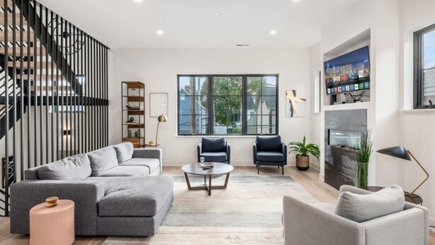 Uma sala de estar moderna com um sofá cinzento, duas poltronas, uma mesa de centro e uma escada com guarda-corrimão preto.