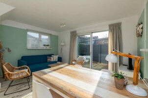 Uma sala de estar com um sofá azul, mesa de centro de madeira, cadeiras de vime e uma luminária de mesa.