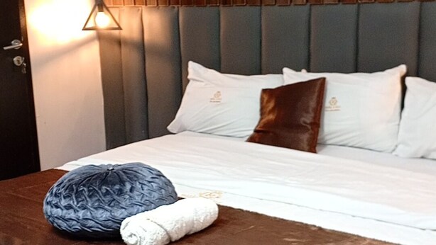 Cama bem arrumada com cabeceira marrom, roupa de cama branca e travesseiro azul.