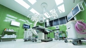 Uma sala de operações moderna com paredes verdes, luzes cirúrgicas e equipamentos médicos.