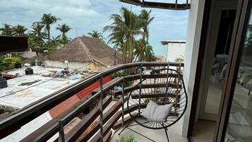 Uma varanda com pérgola de madeira, uma mesa redonda com uma planta e uma cadeira preta.