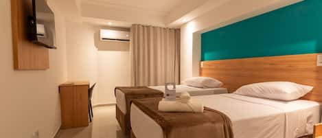 Quarto de hotel com uma cama, escrivaninha, cadeira, televisão e ar condicionado.