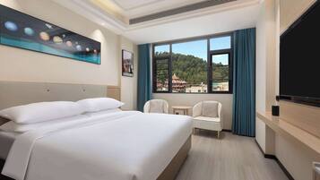 Quarto de hotel com uma cama grande, televisão, uma mesinha e janela com vista para um edifício tradicional.