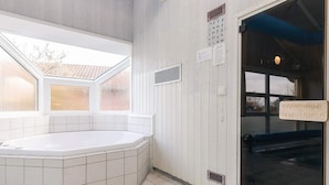 Um quarto de spa com uma banheira grande, um claraboia e uma placa indicando uma sauna.