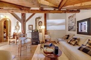 Uma sala de estar aconchegante com vigas de madeira, um sofá, cadeiras, uma mesa de centro e uma lareira.