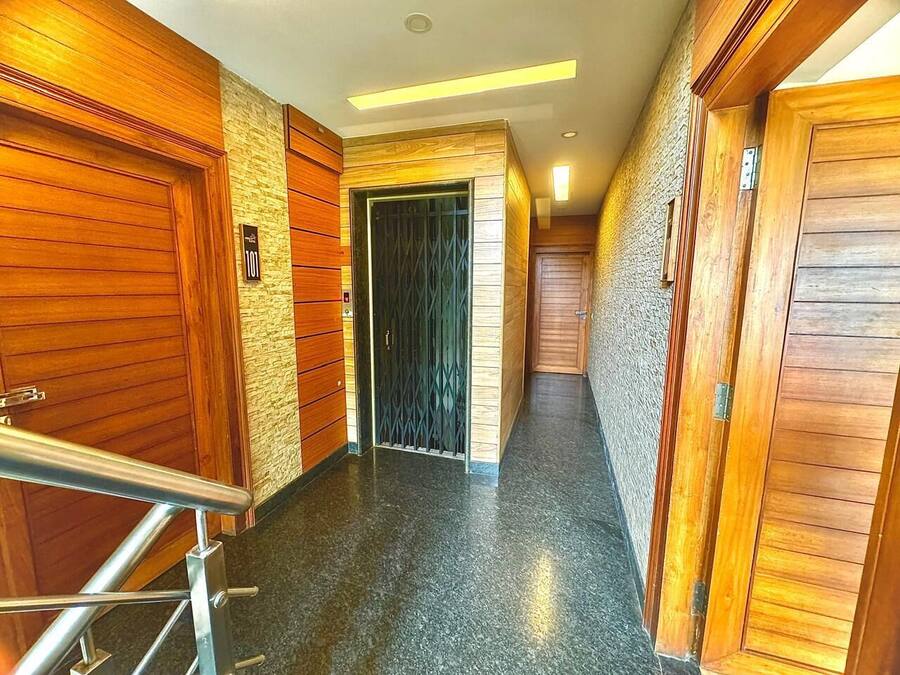 Corredor de hotel com portas de madeira, corrimão de metal e parede texturizada.