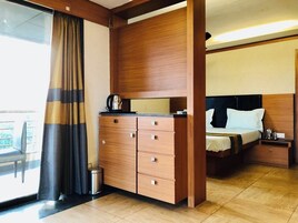 Quarto de hotel com penteadeira de madeira, cama com cabeceira preta e janela com cortinas.