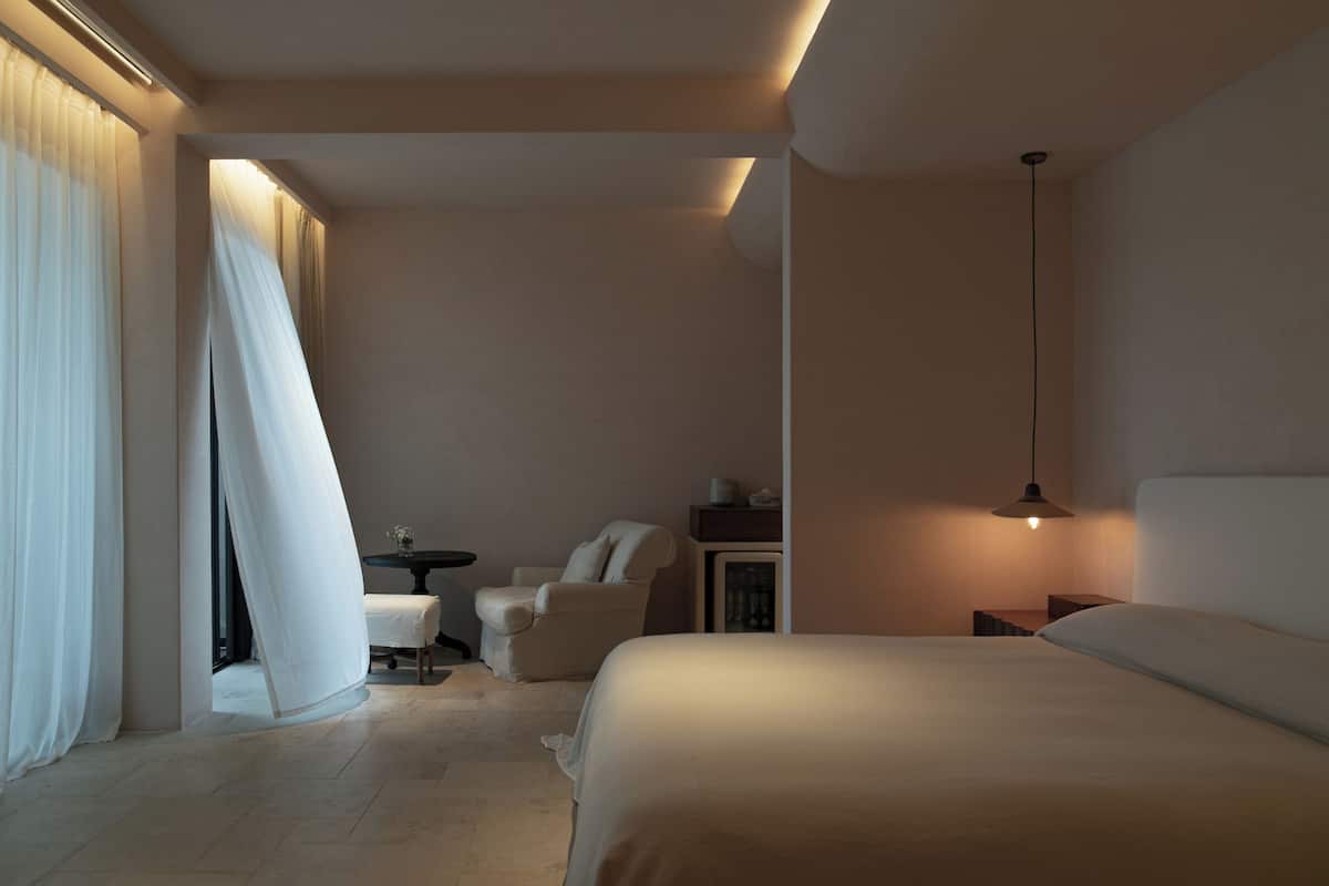 Quarto de hotel moderno com uma cama grande, uma escrivaninha, uma cadeira e uma mesinha.
