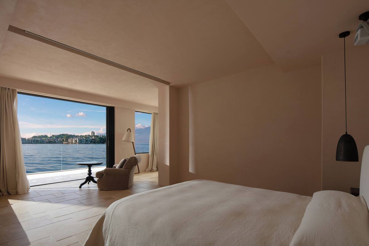 Um quarto espaçoso com uma cama grande, vista para o mar, uma mesinha e uma cadeira.