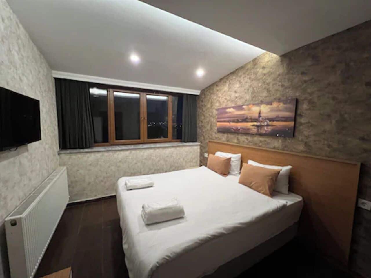 Quarto de hotel com uma cama grande, televisão de tela plana na parede, janela com cortinas e um quadro na parede.