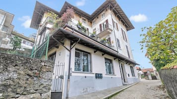 Um edifício de dois andares com fachada de pedra, uma varanda com plantas e uma rua de paralelepípedos.