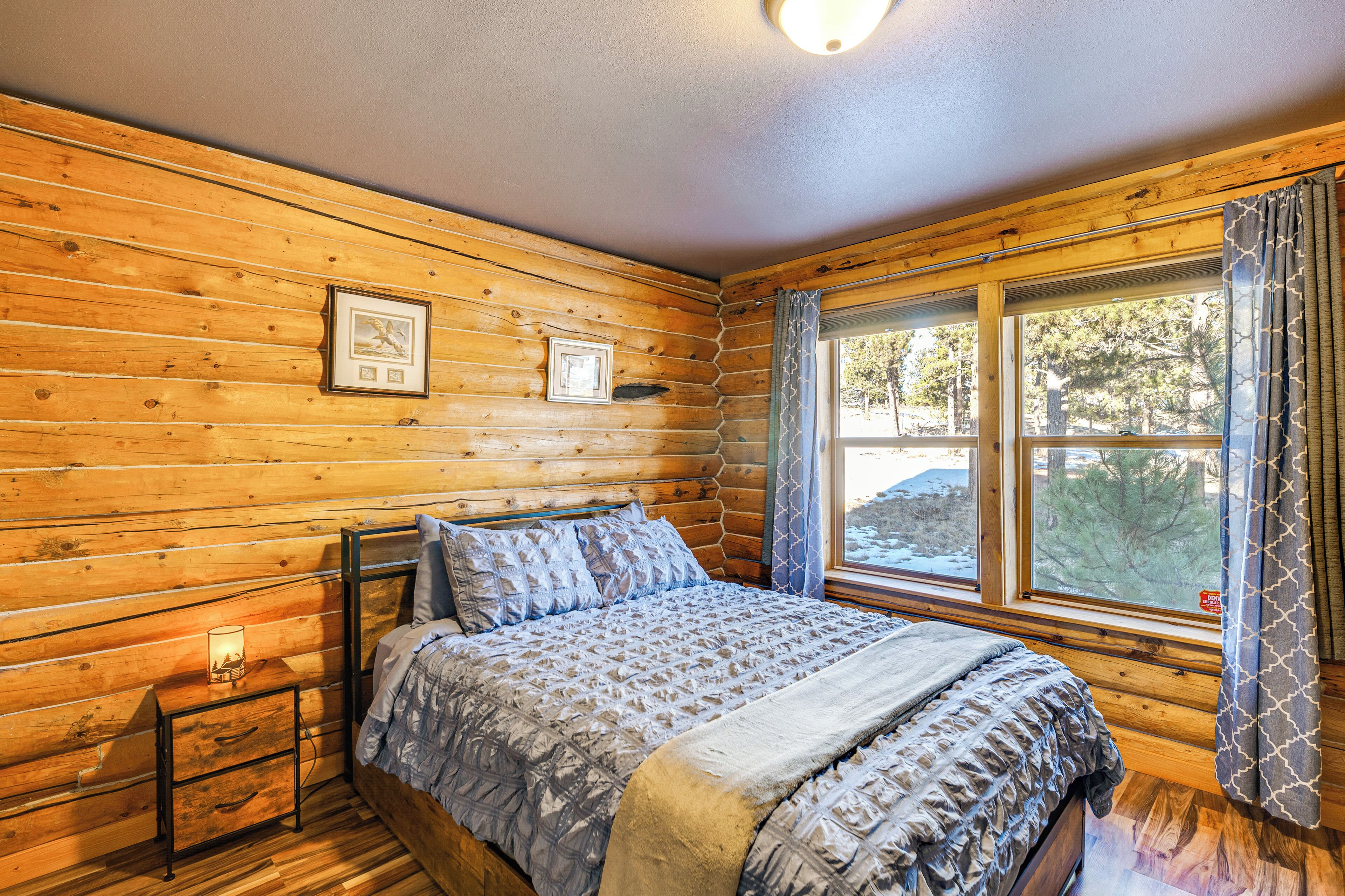 Quarto de cabana de madeira com uma cama, mesa de cabeceira e janela com cortinas.
