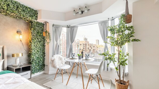 Quarto moderno com vista para a cidade, uma mesa redonda com cadeiras, uma cama e uma janela grande com cortinas.