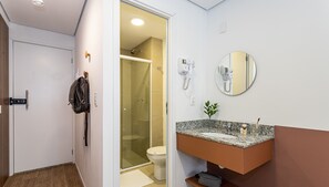 Casa de banho moderna com chuveiro de vidro, sanita branca, toucador com bancada de granito e espelho.
