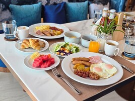 Um buffet de café da manhã com diversos pratos, incluindo ovos, linguiça e pães, além de bebidas e acompanhamentos.