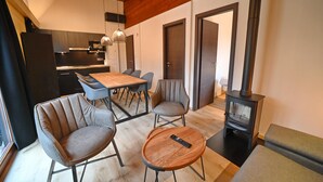 Uma cozinha moderna com armários escuros, uma mesa de jantar de madeira e um fogão embutido. Há duas cadeiras e um controle remoto sobre a mesa.