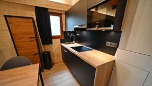 Cozinha compacta com armários escuros, bancada de madeira e janela com cortinas.