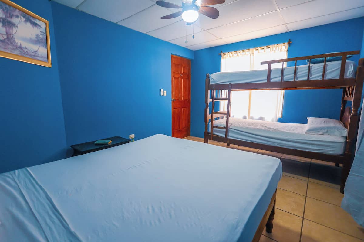 Quarto com cama de solteiro, beliche e ventoinha de teto.