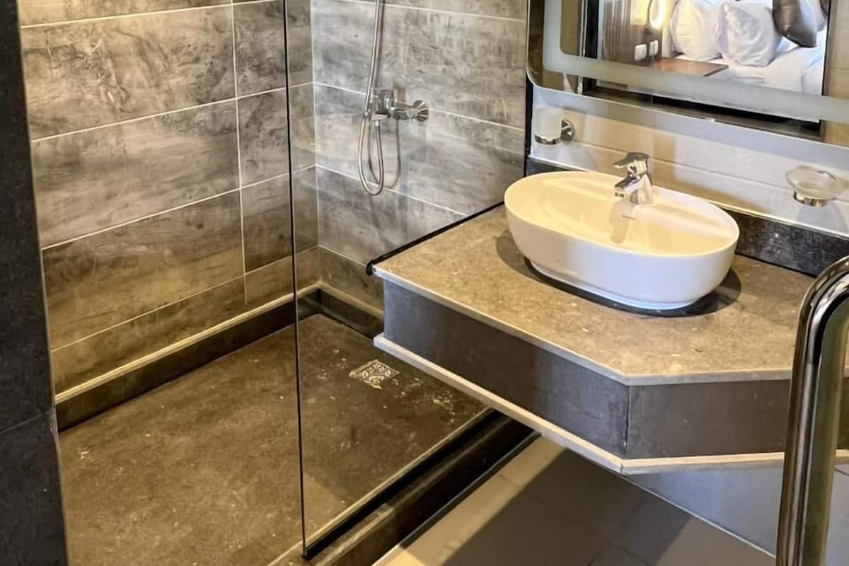 Um banheiro moderno com chuveiro em cabine de vidro, pia com bancada e um espelho grande acima do armário.