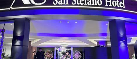 A entrada do Hotel San Stefano, com um destaque para o logotipo 'XU' e um design moderno com iluminação azul.