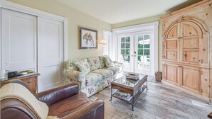 Uma sala de estar com um sofá de couro marrom, um sofá estampado com flores, uma mesa de centro de vidro e um armário de madeira.
