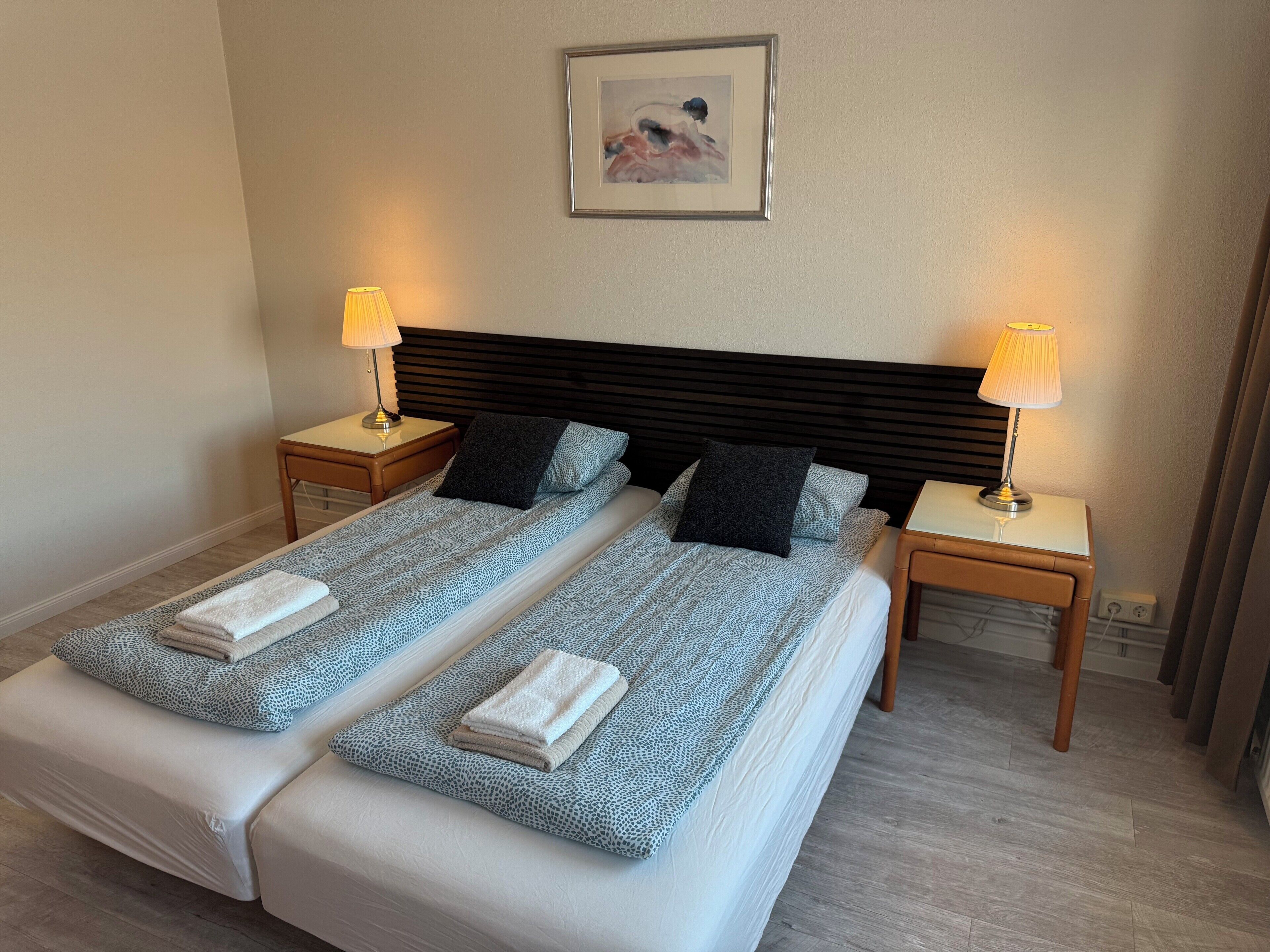 Uma cama de casal com duas almofadas e duas mesas de cabeceira, cada uma com uma luminária.