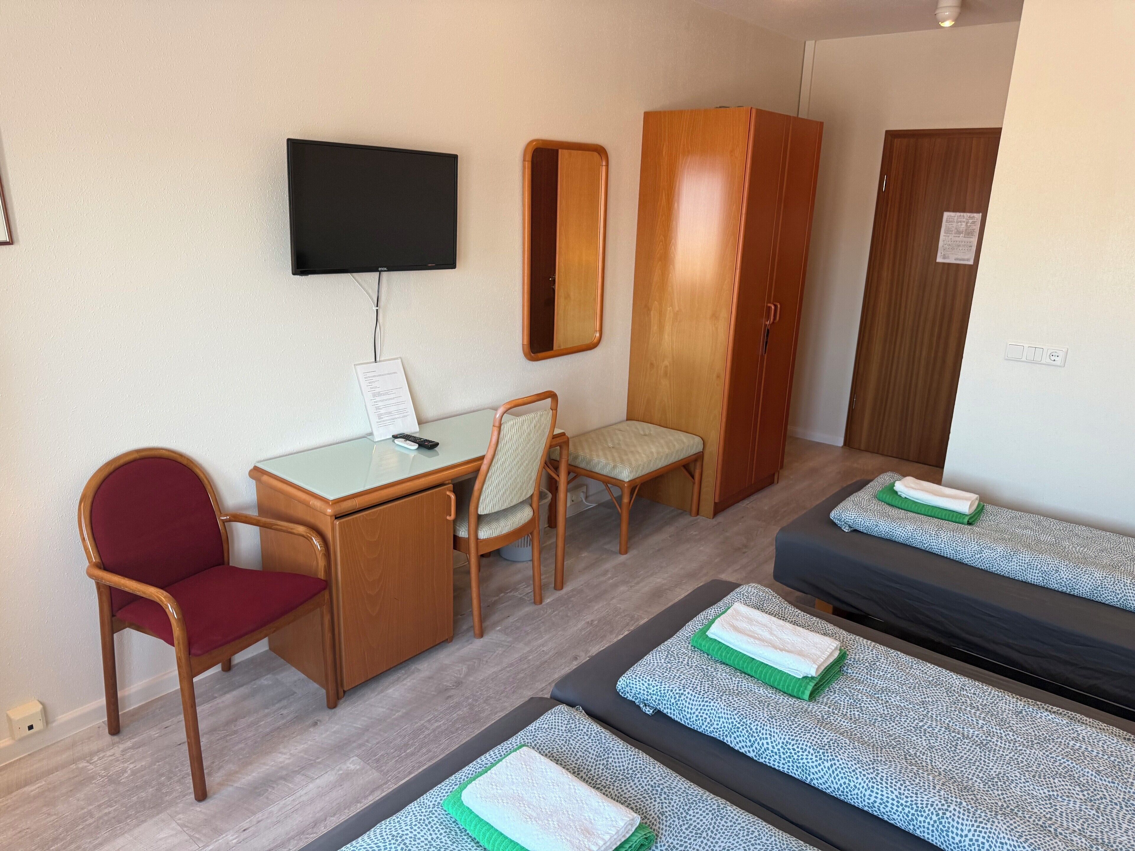 Quarto de hotel com escrivaninha, cadeira, televisão, guarda-roupa e duas camas.