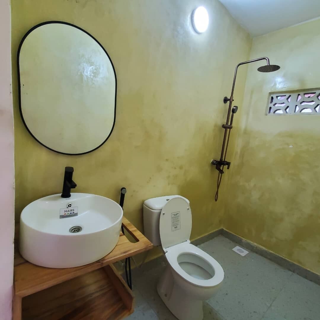 Um banheiro pequeno com um espelho redondo, uma pia branca, vaso sanitário e chuveiro.