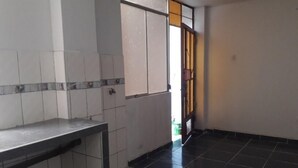 Um corredor com paredes e chão de azulejos, uma porta com grades de metal e um balcão com puxador.
