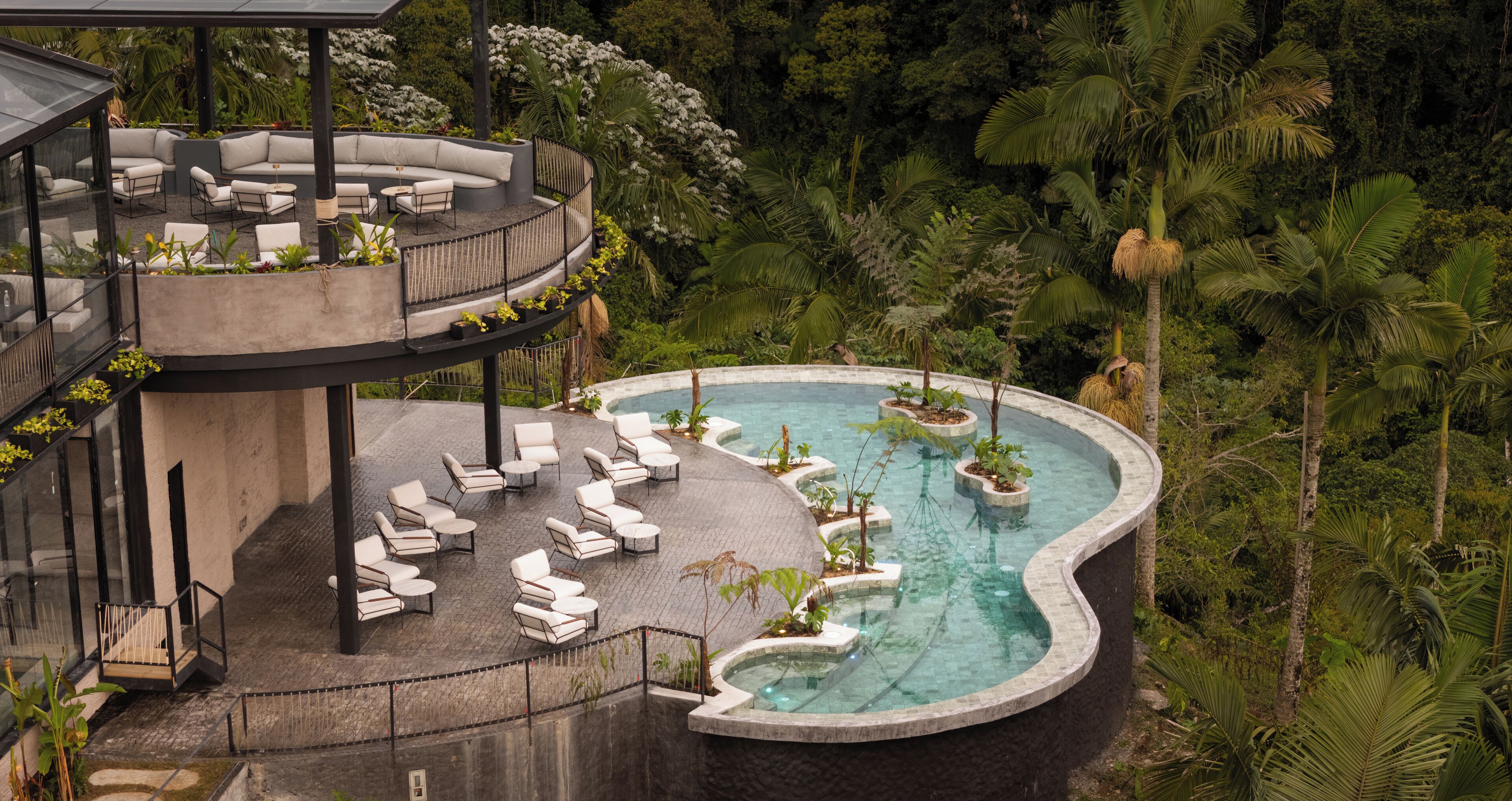 Uma área de piscina no terraço com espreguiçadeiras e uma piscina circular rodeada por vegetação exuberante.