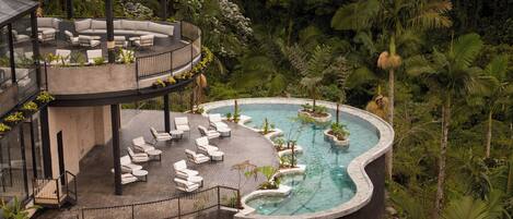 Uma área de piscina no terraço com espreguiçadeiras e uma piscina circular rodeada por vegetação exuberante.