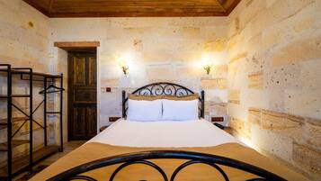 Quarto com cama, cabeceira de madeira, paredes de pedra e teto de madeira.