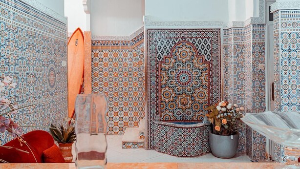Um quarto com padrões de azulejos elaborados, uma planta em vaso e uma cadeira vermelha.