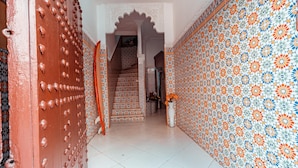 Um corredor com papel de parede estampado, escada e porta com detalhe decorativo.