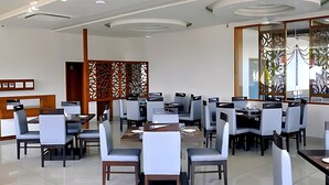 Uma área de refeições moderna com várias mesas e cadeiras, um painel decorativo e iluminação embutida no teto.