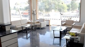 Sala de estar moderna com sofá, duas mesinhas de centro e vista da rua através de grandes janelas.