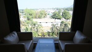 Quarto com mesa de vidro e dois sofás voltados para a vista de uma paisagem urbana com edifícios e árvores.