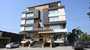 Um hotel de vários andares com design moderno, apresentando uma área de recepção, uma escadaria que leva à entrada e um estacionamento com carros.