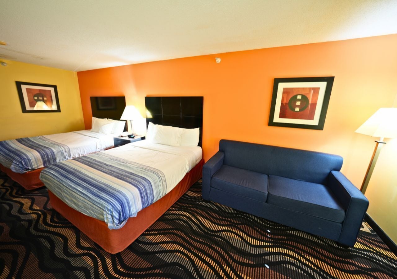 Quarto de hotel com duas camas, um sofá azul e um tapete estampado.