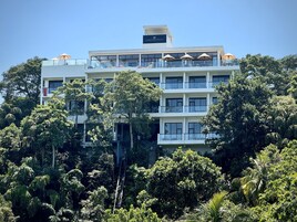 Um hotel com vários andares e varandas, rodeado por vegetação densa.