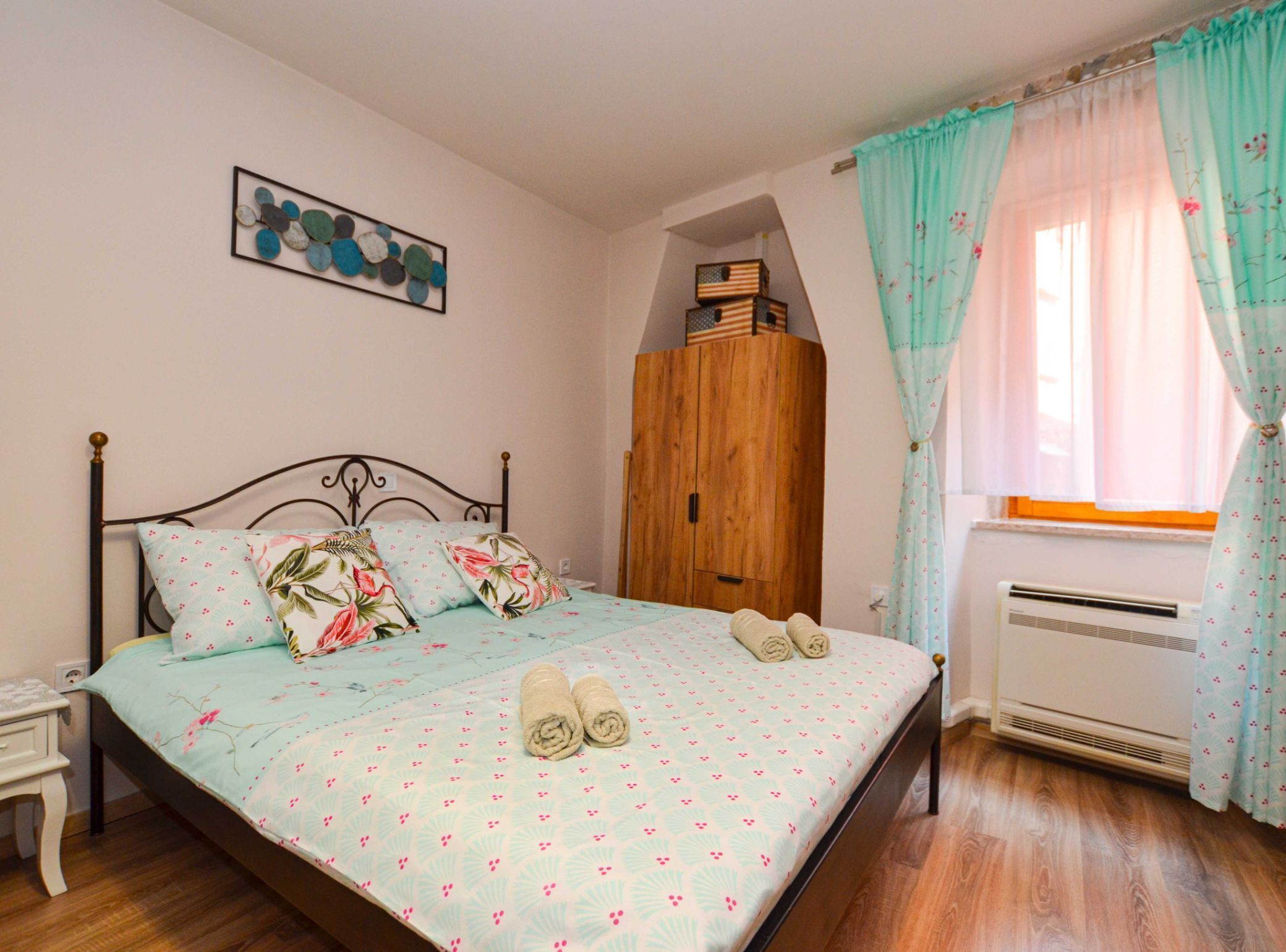 Quarto com cama, guarda-roupa de madeira, mesa de cabeceira e janela com cortinas.