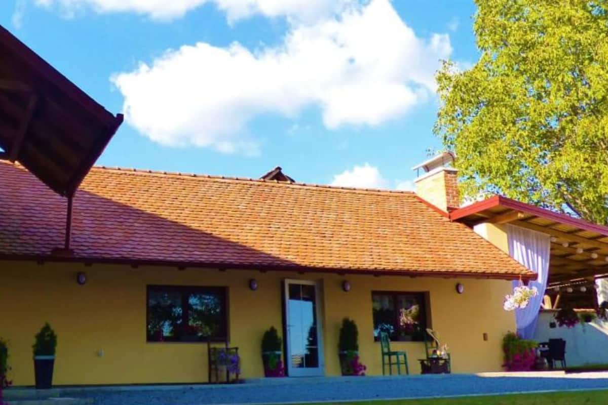 Um edifício amarelo com telhado telhado, varanda coberta e uma árvore ao fundo.