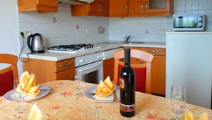 Uma cozinha com armários de madeira, fogão a gás, micro-ondas e uma mesa de jantar posta com pratos, guardanapos e uma garrafa de vinho.